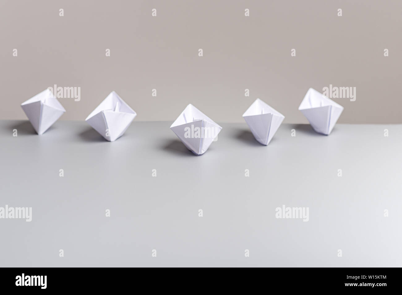 Five white origami paper boats on white desk over grey background. With ...