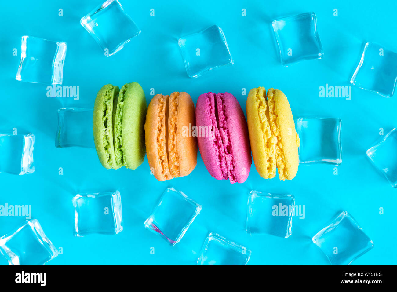 Flat lay of colorful macaroons and ice cubes against blue background ...