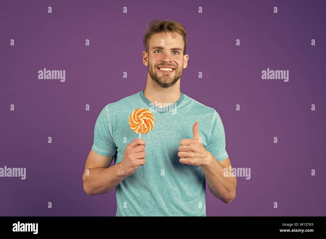 Guy hold lollipop candy violet background. Man handsome macho eat big ...