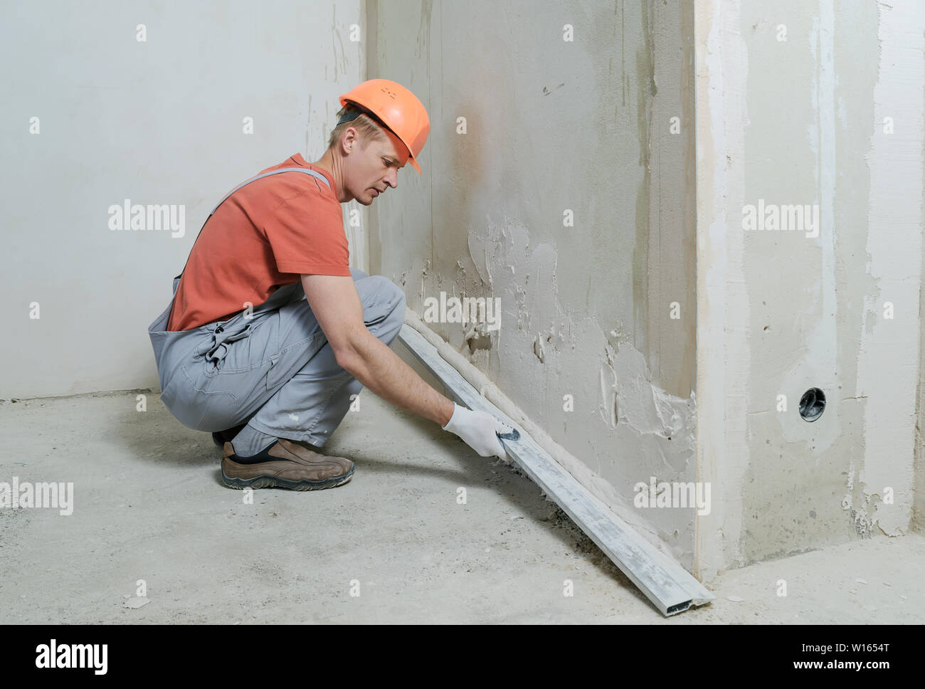Worker is putting a gypsum plaster on a wall. He is using a long rulerl ...