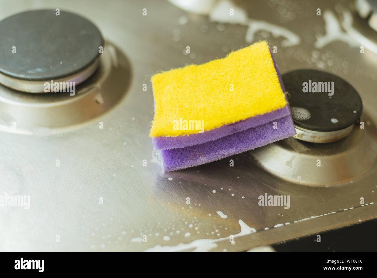 Violet - yellow sponge with a metal gas stove. Cleaning the dirt with a ...