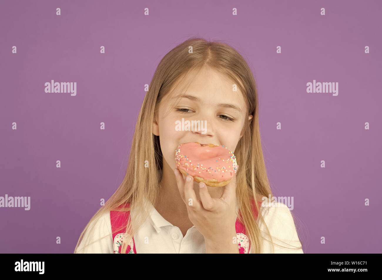 Child eat donut on violet background. Little girl bite glazed ring ...