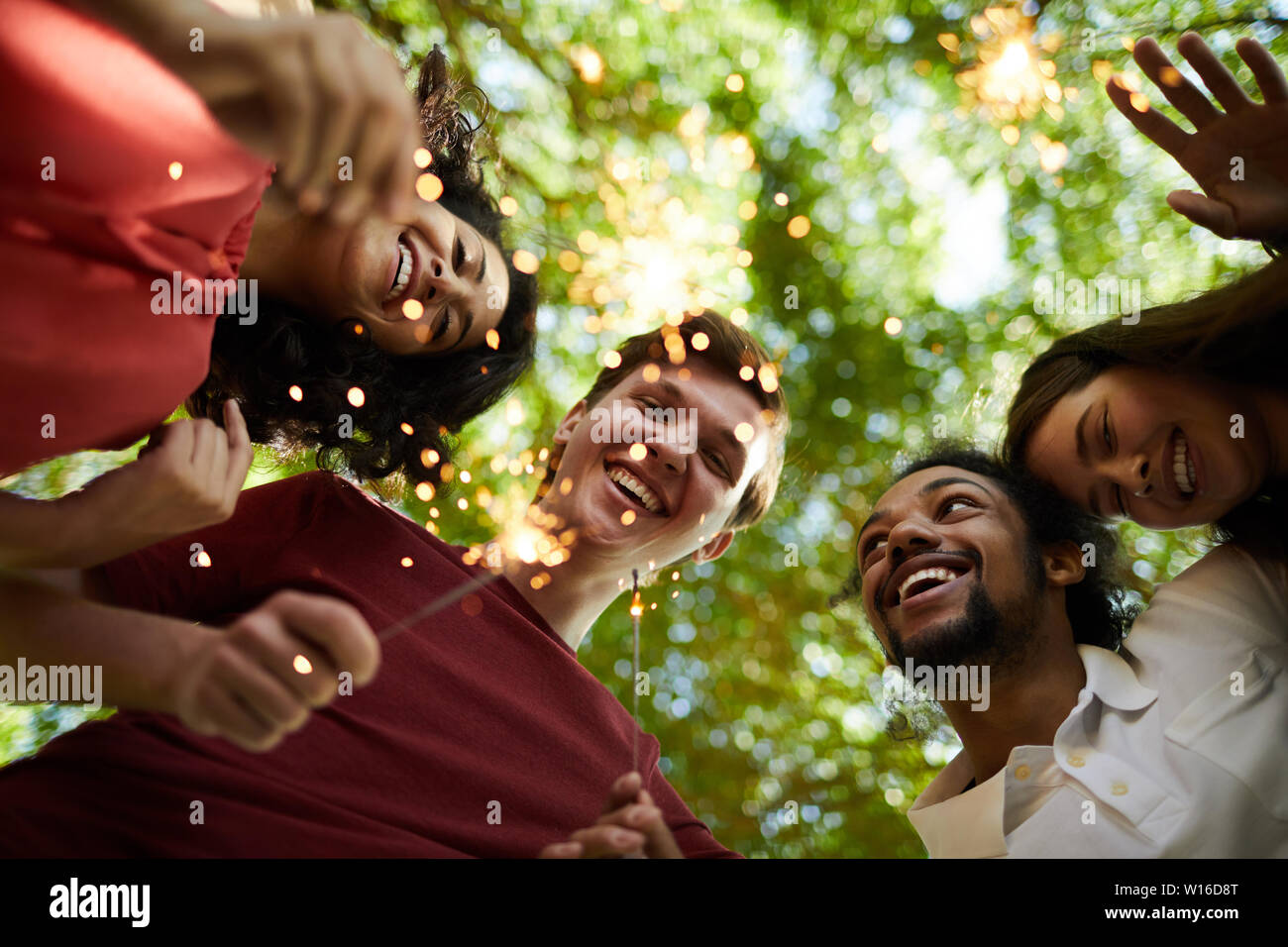 Low angle portrait of friends holding sparkling lights outdoors while ...