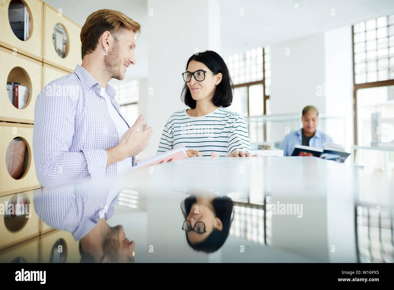 Positive friendly young bookstore clerk gesturing hand while sharing ...