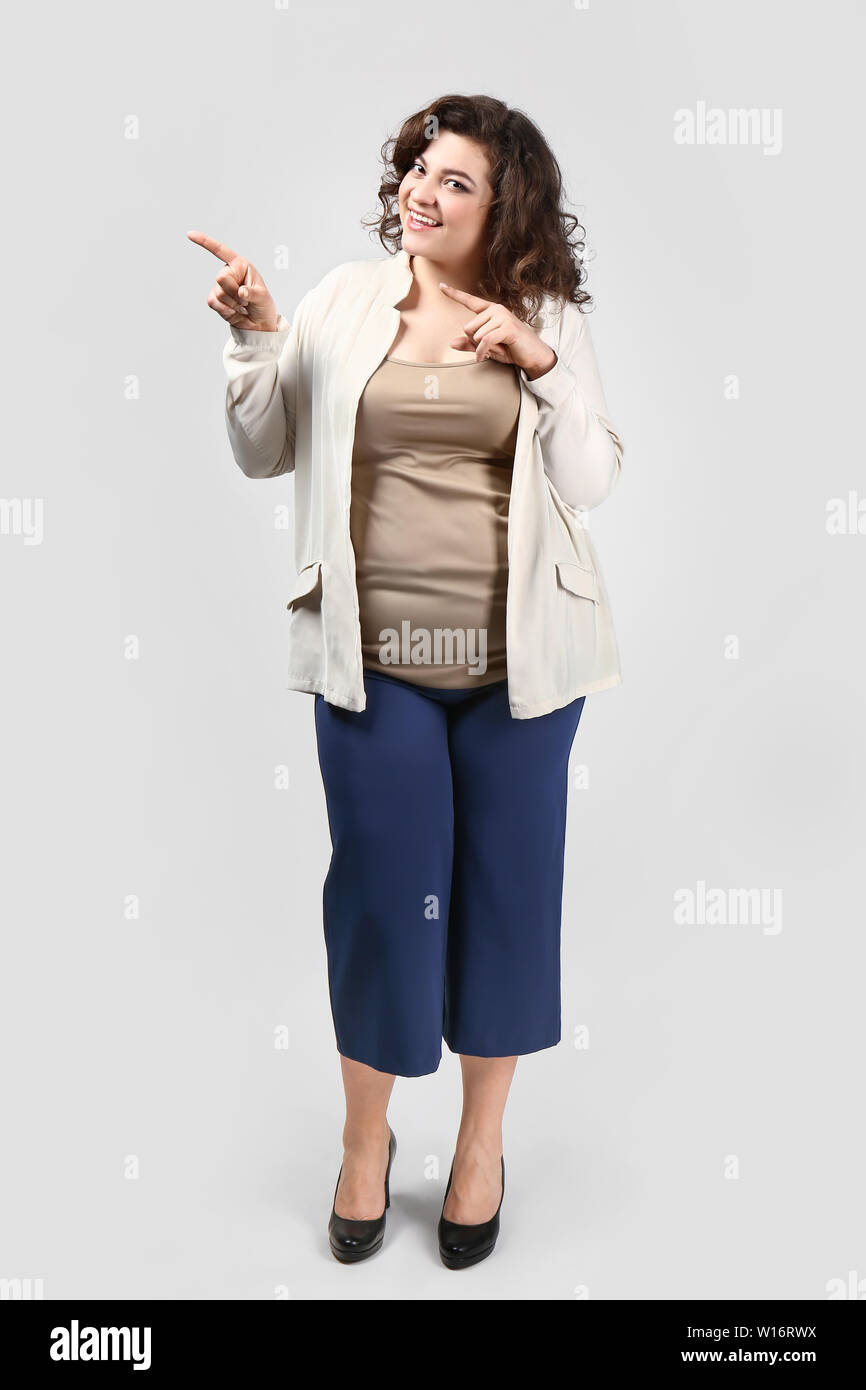 Stylish overweight woman pointing at something on light background ...
