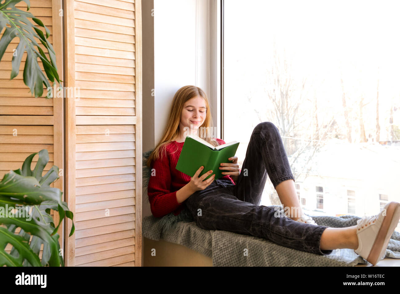 Cute teenage girl reading book on window sill at home Stock Photo - Alamy