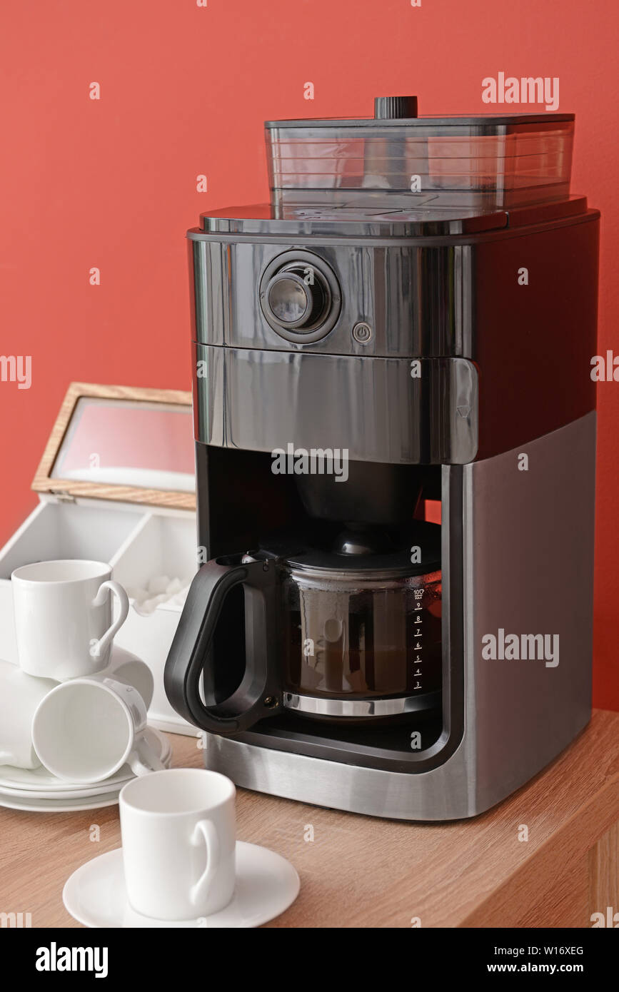 Modern coffee machine and cups on table against color background Stock ...