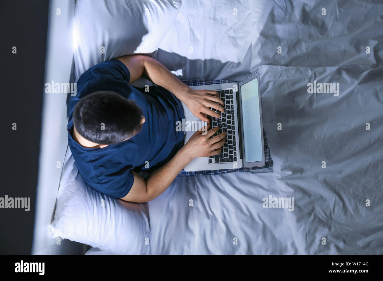 Young man with laptop in bed at night, top view Stock Photo - Alamy