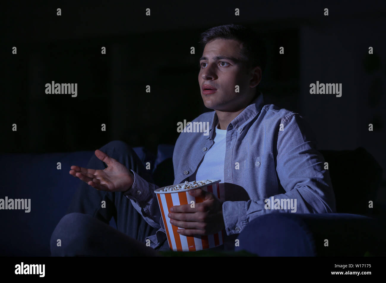 Young man eating popcorn while watching TV late at night Stock Photo ...