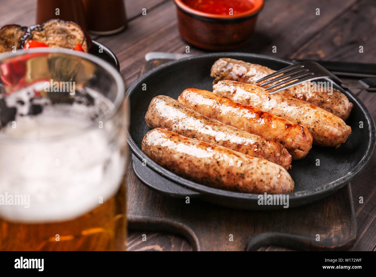 Frying pan with tasty grilled sausages and beer on wooden table Stock ...