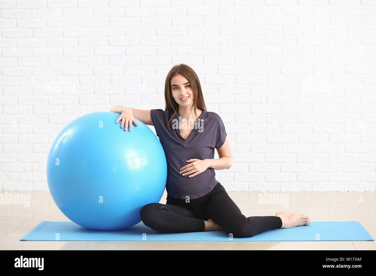 Beautiful pregnant woman with fitball training near white brick wall ...