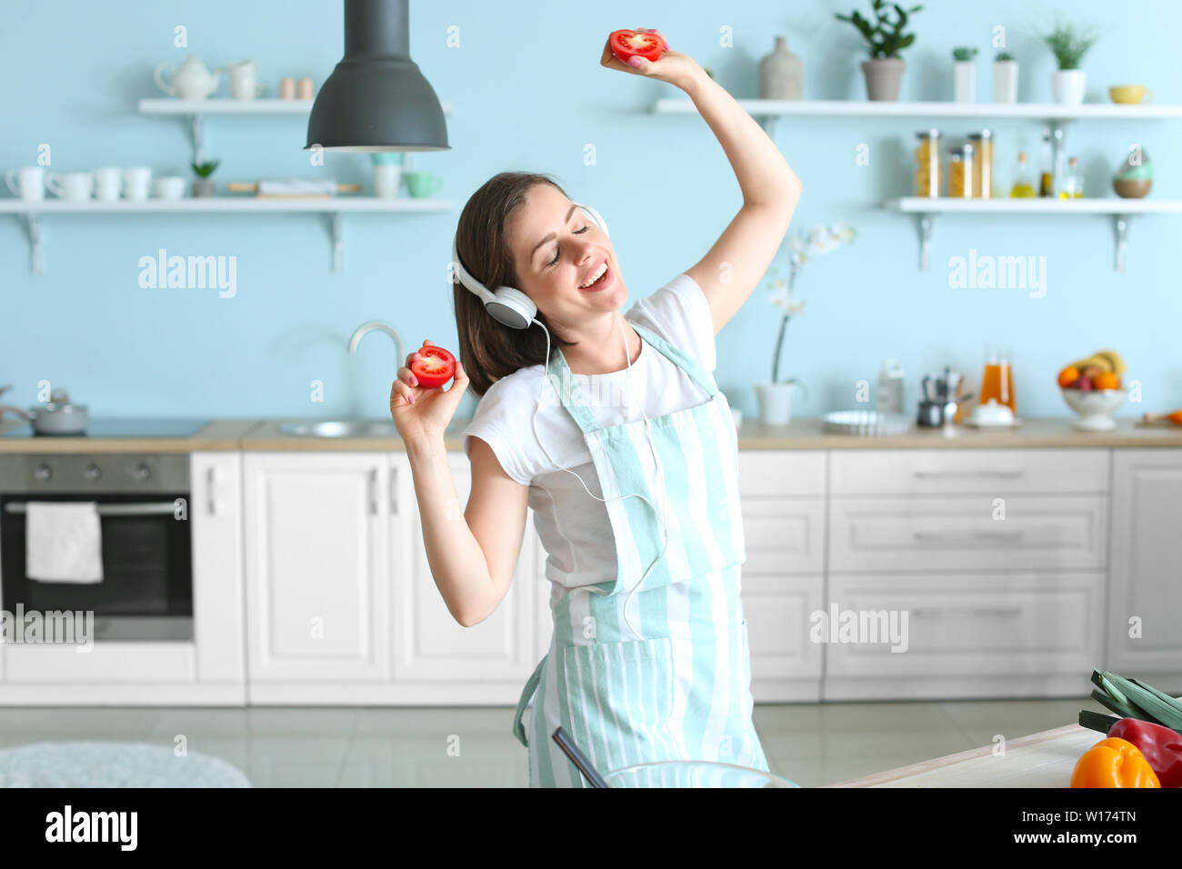 Beautiful young woman listening to music and dancing while cooking in ...