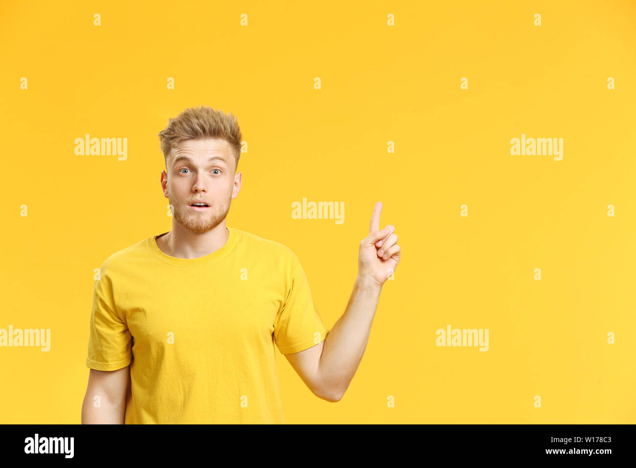 Portrait of scared young man pointing at something on color background ...