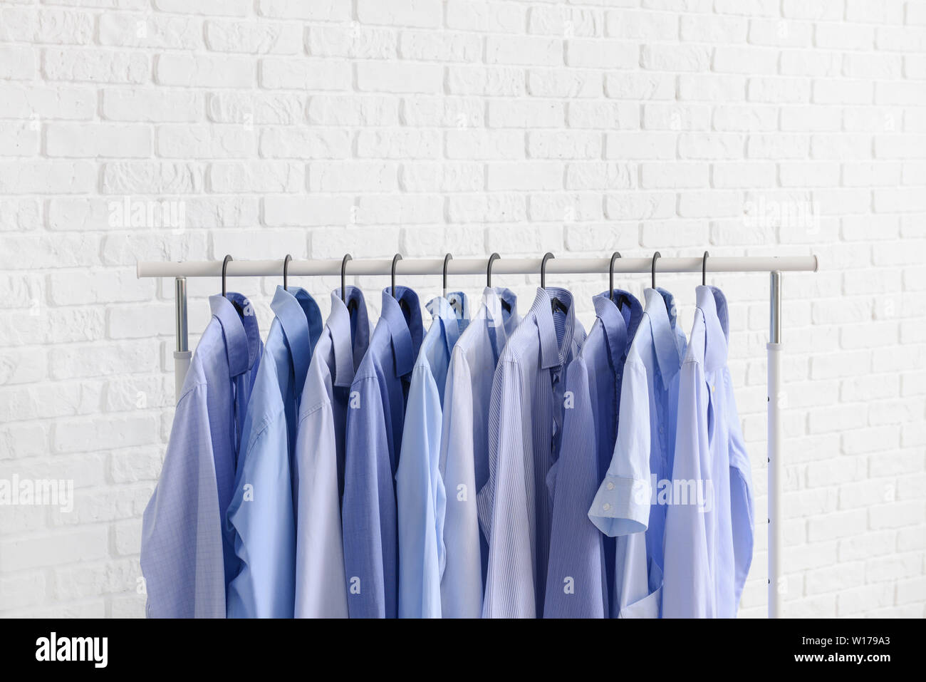 Rack with clothes after dry-cleaning near white brick wall Stock Photo ...