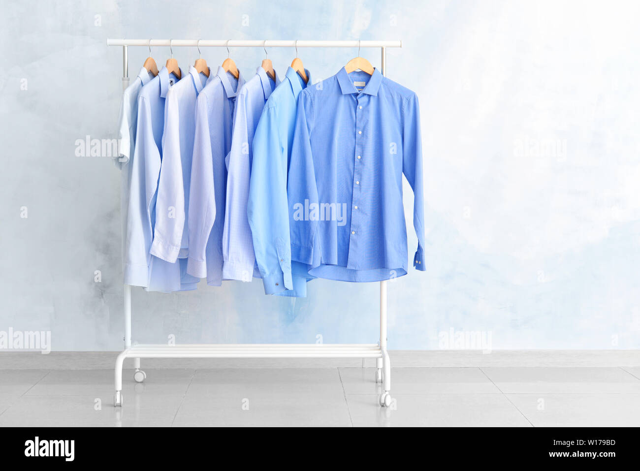Rack with clothes after dry-cleaning near light wall Stock Photo - Alamy