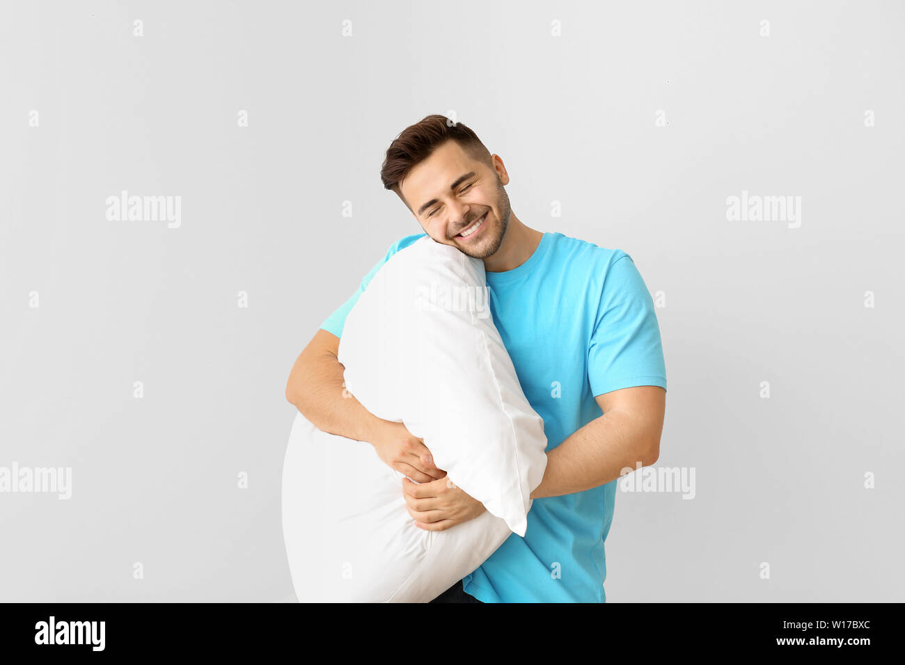 Handsome man hugging pillow against white background Stock Photo - Alamy