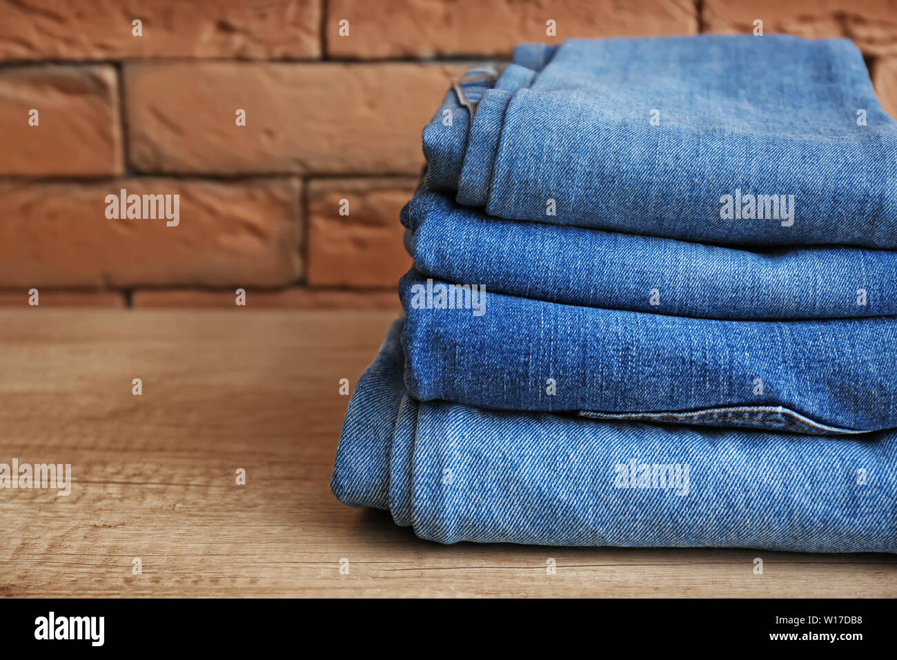 Stack of jeans clothes on table against brick wall Stock Photo - Alamy