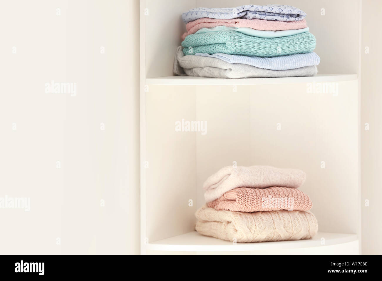 Rack with stacks of clean clothes near white wall Stock Photo - Alamy