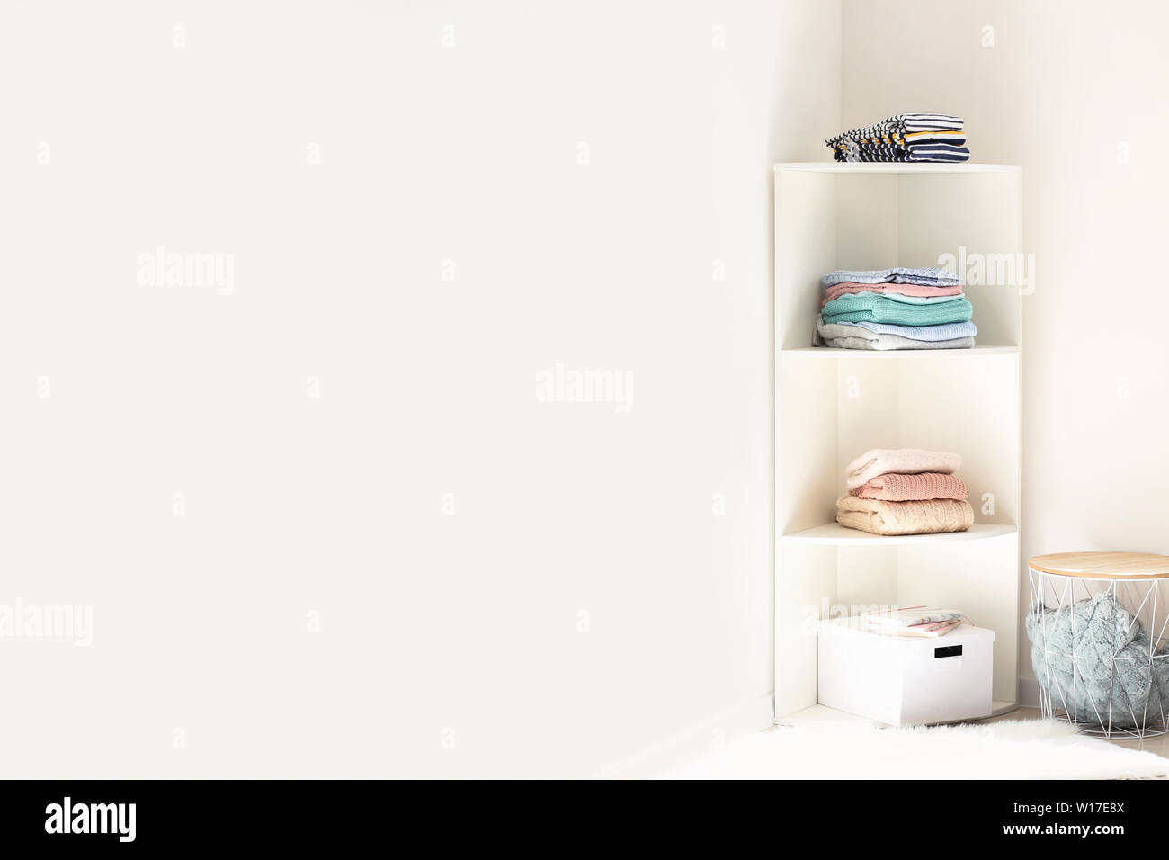 Rack with stacks of clean clothes near white wall Stock Photo - Alamy