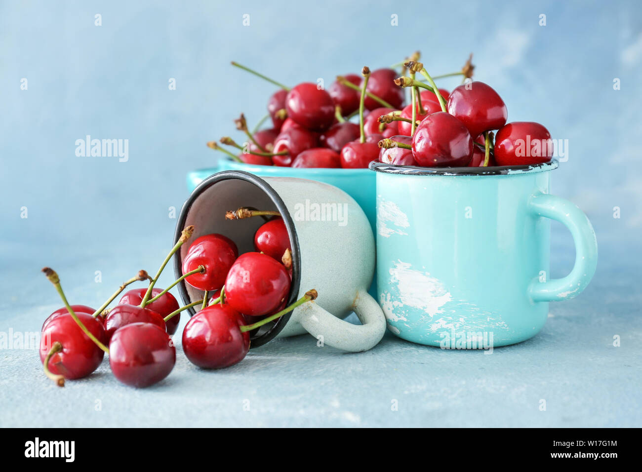 Mugs and pot with sweet ripe cherry on color background Stock Photo - Alamy