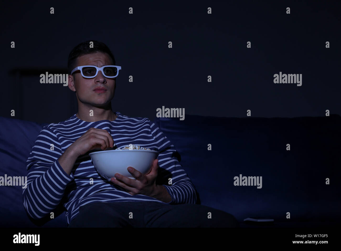 Young man eating popcorn while watching TV late at night Stock Photo ...