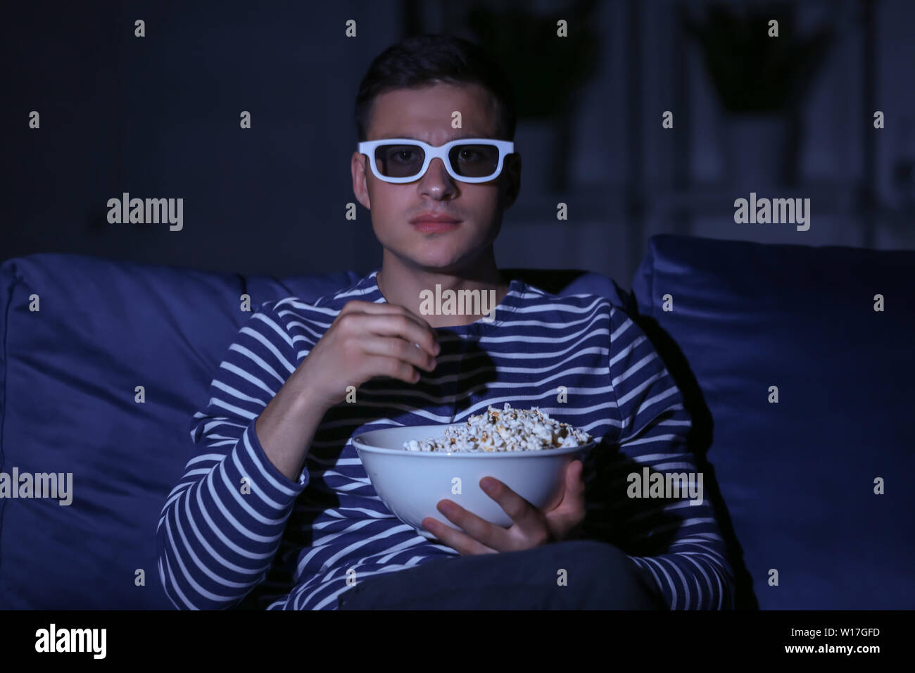 Young man eating popcorn while watching TV late at night Stock Photo ...