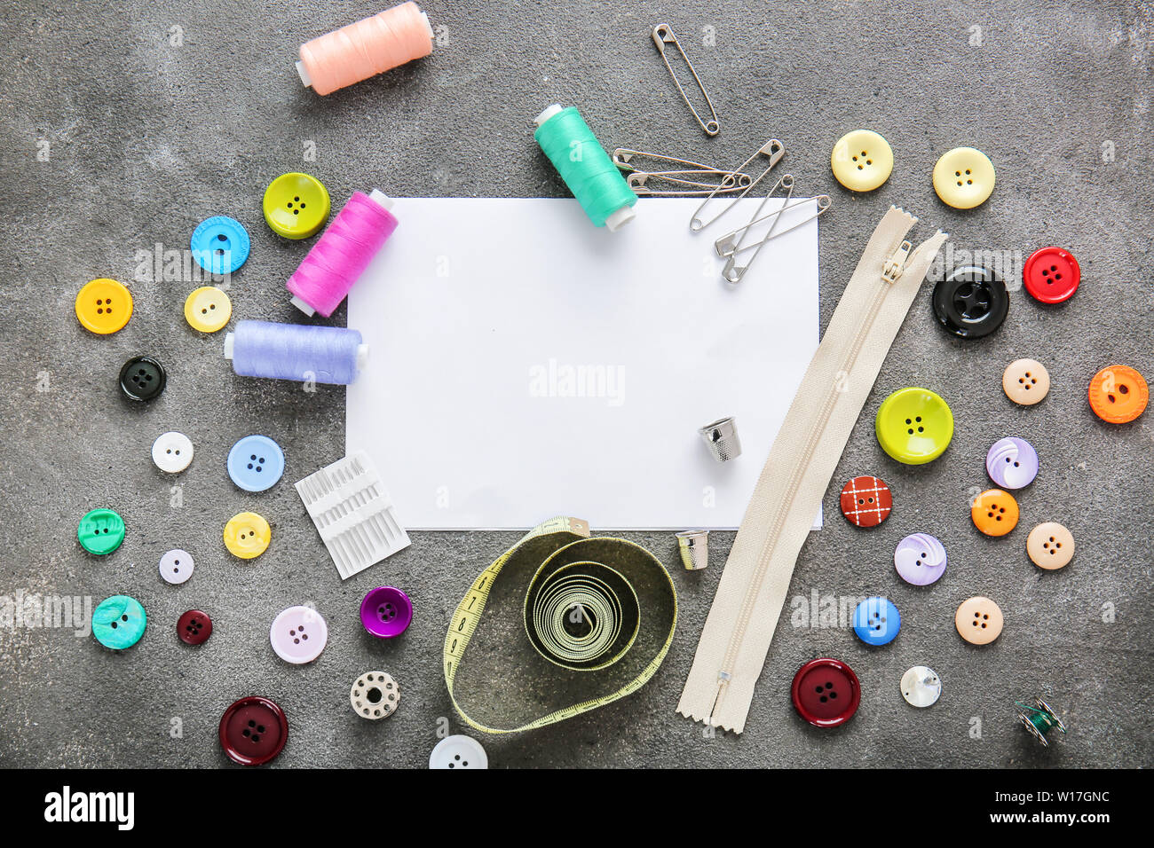Set of sewing threads with accessories and sheet of paper on grey ...