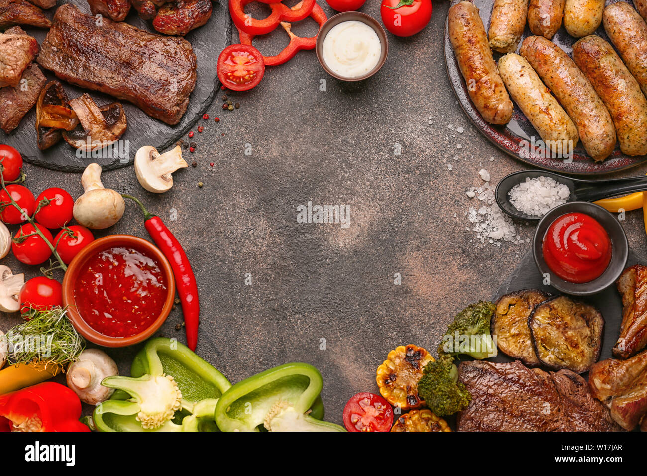 Frame made of tasty grilled meat with sausages and vegetables on grey ...