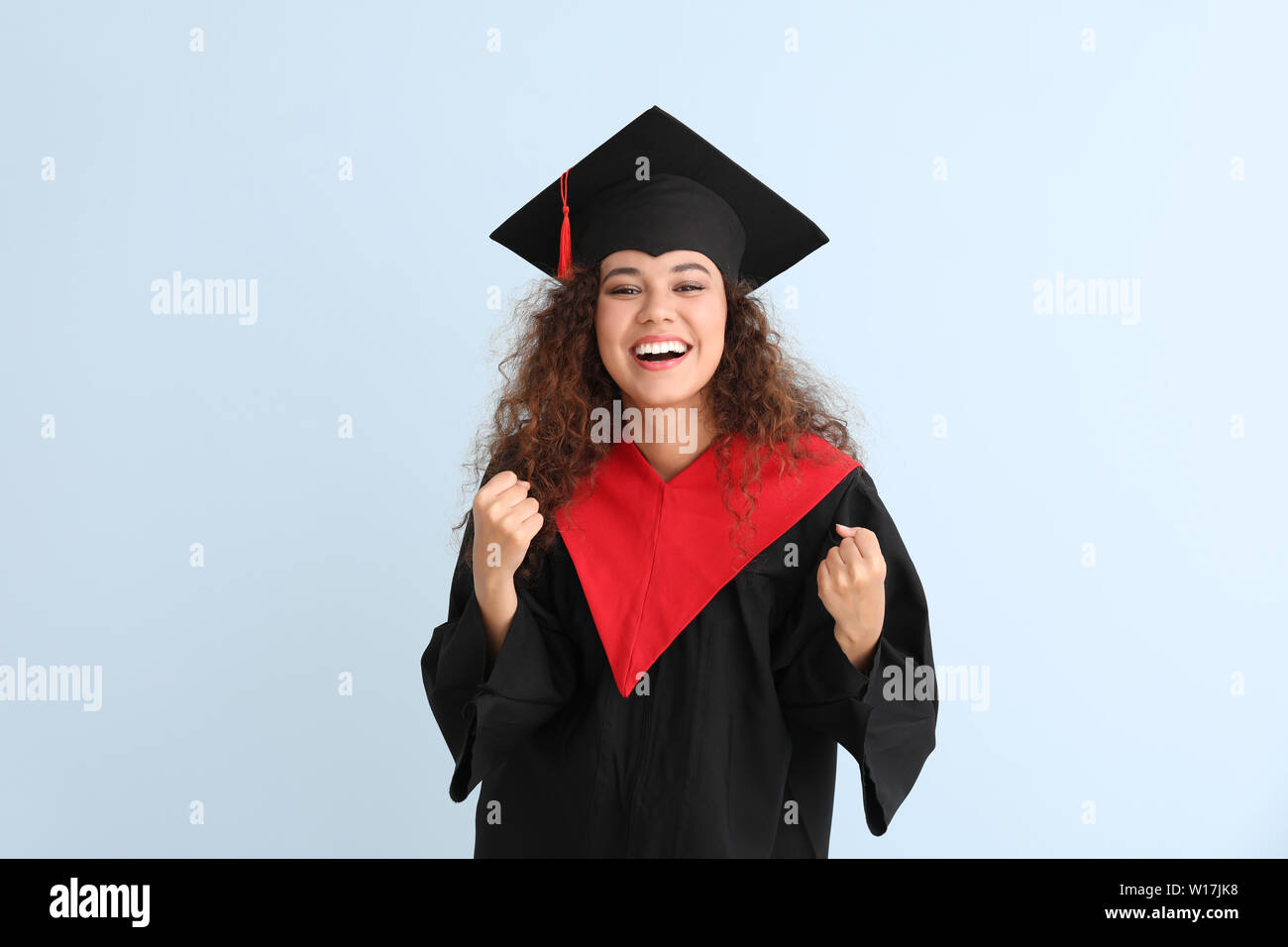 Happy African-American student in bachelor robe on color background ...