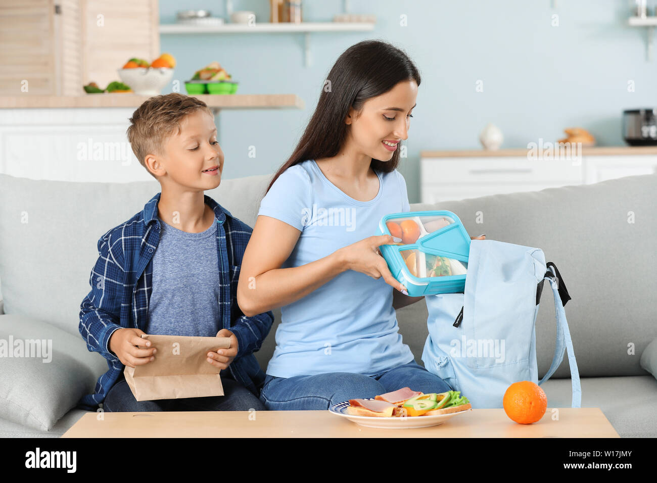 Mother putting lunch box into backpack of her little son before school ...