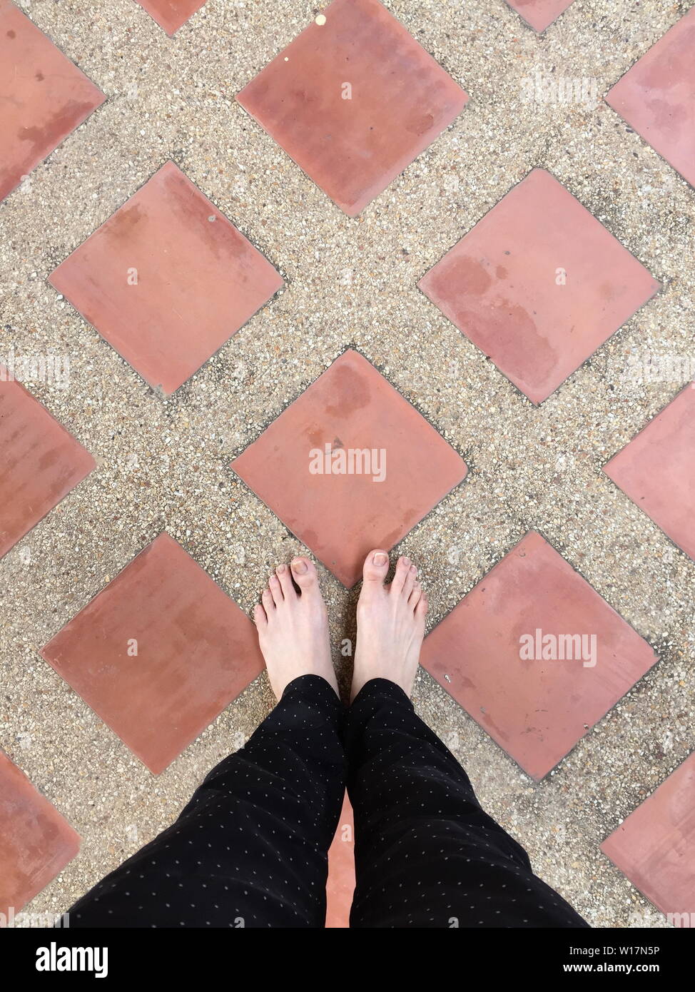 Feet on orange tile floor. Young woman barefoot or feet standing on the ...