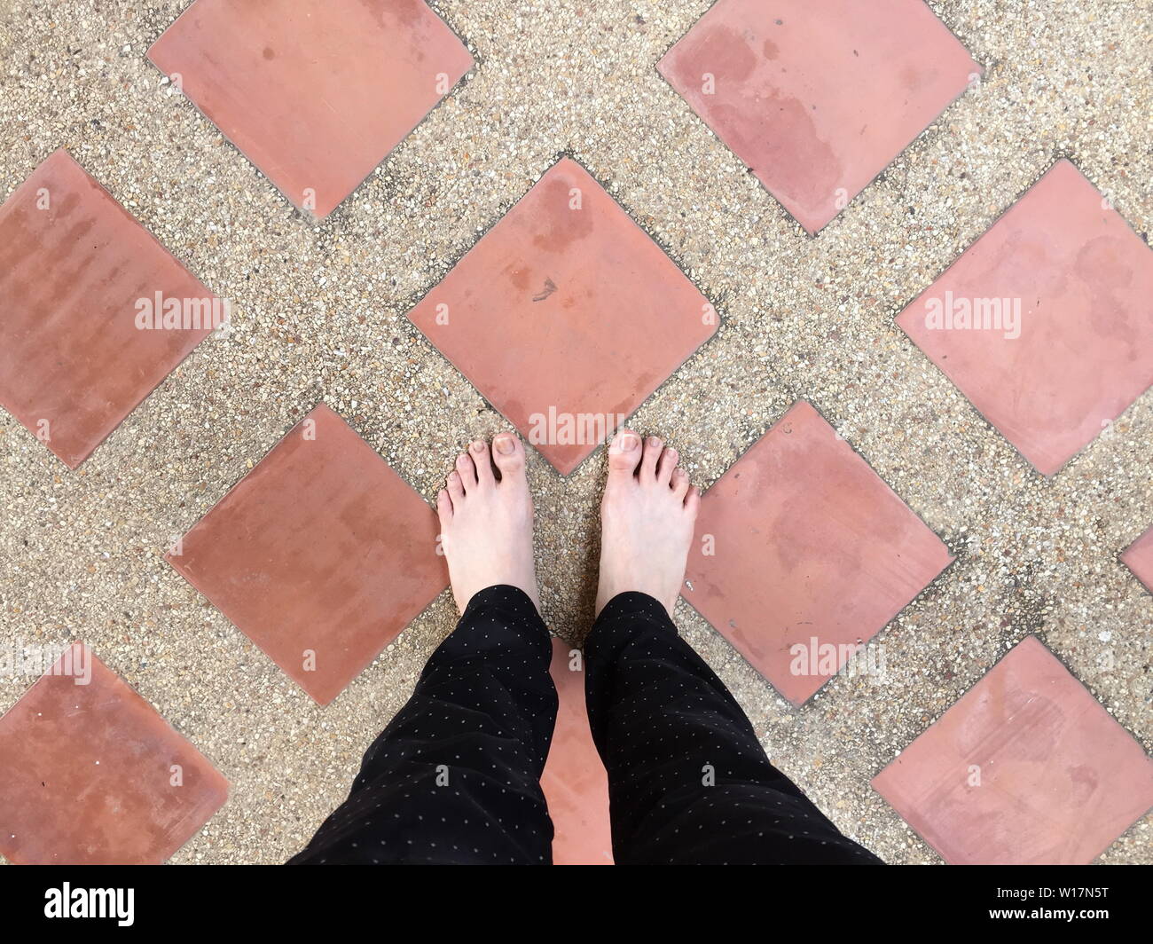Feet on orange tile floor. Young woman barefoot or feet standing on the ...
