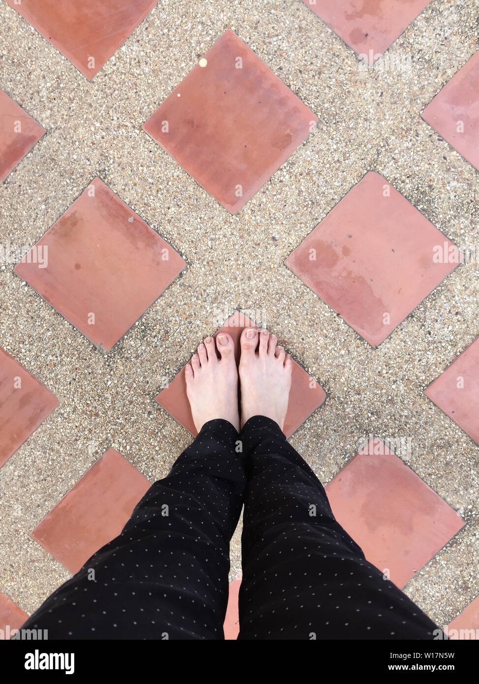 Feet on orange tile floor. Young woman barefoot or feet standing on the ...
