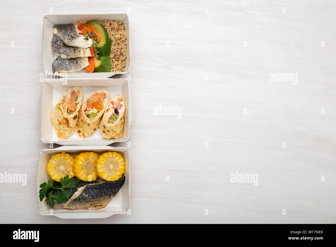 Three kinds of lunch boxes with fish and vegetables lie on a white ...