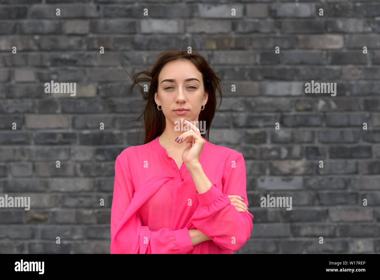 Thoughtful woman standing staring at the camera with her hand to her ...
