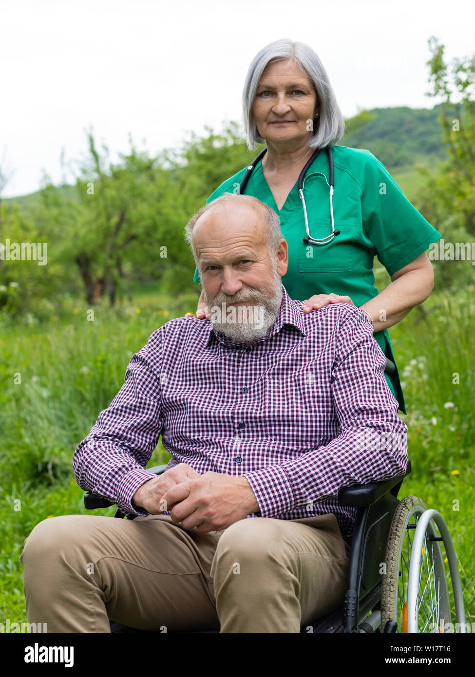Portrait of a mature invalid man sitting in wheelchair supported by ...