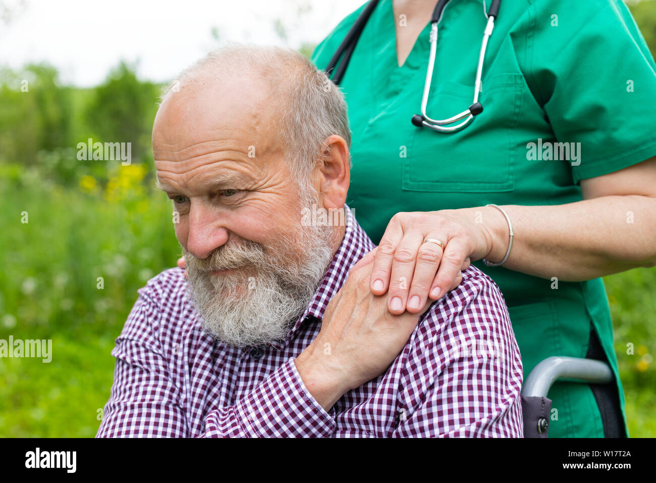 Portrait of a mature invalid man sitting in wheelchair supported by ...