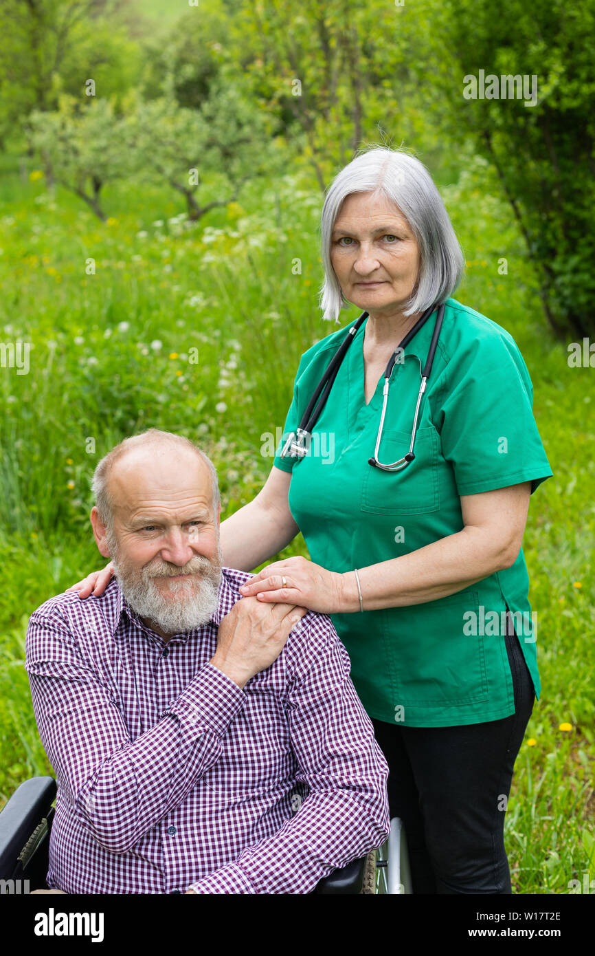 Portrait of a mature invalid man sitting in wheelchair supported by ...