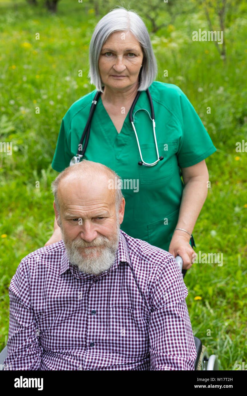 Portrait of a mature invalid man sitting in wheelchair supported by ...