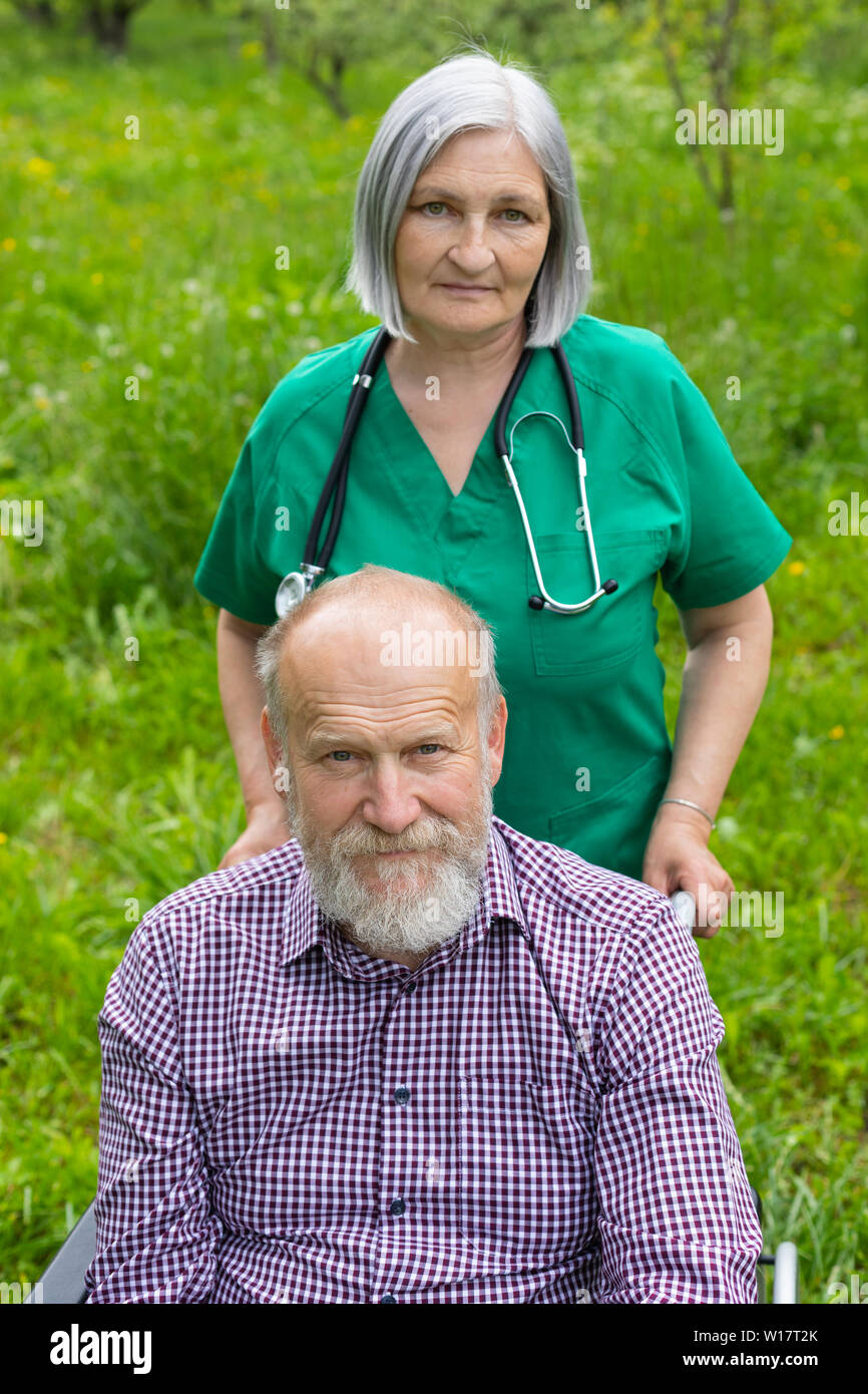 Portrait of a mature invalid man sitting in wheelchair supported by ...