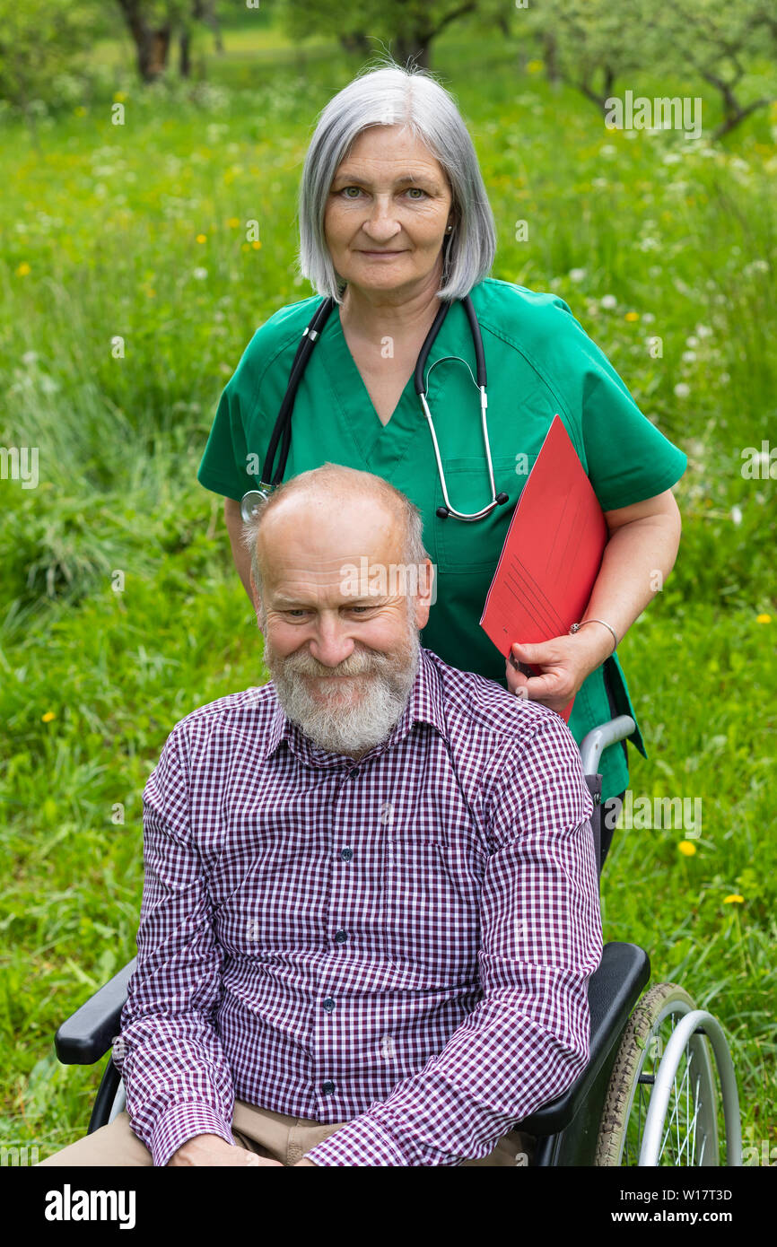 Portrait of a mature invalid man sitting in wheelchair supported by ...