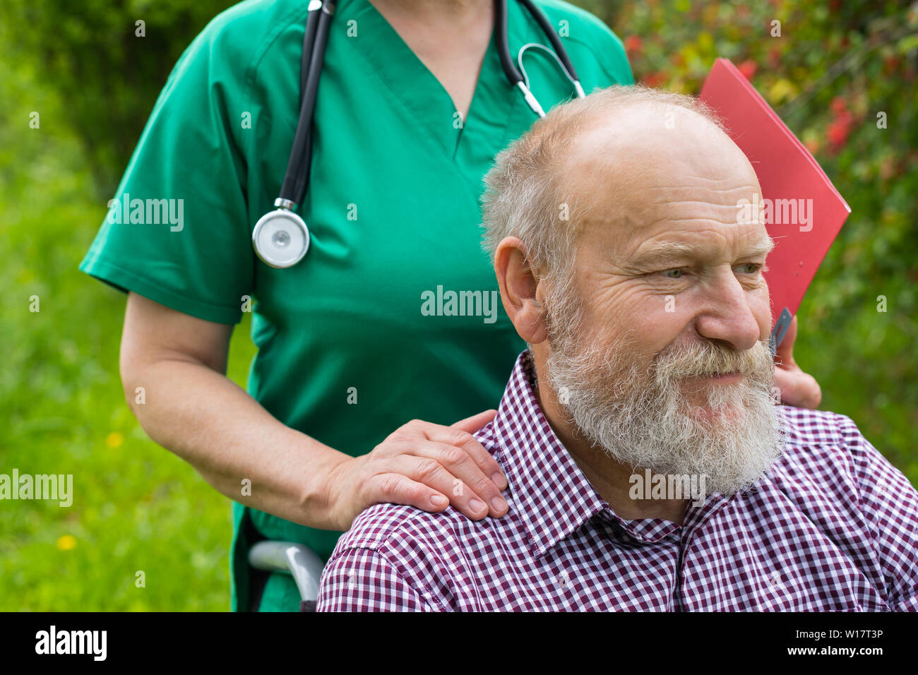 Portrait of a mature invalid man sitting in wheelchair supported by ...
