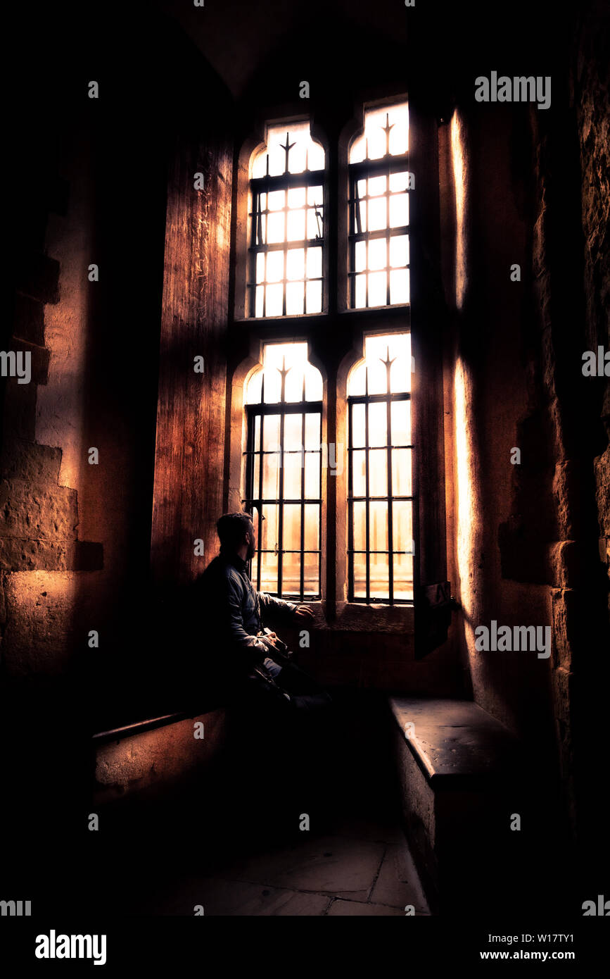 Rear view at silhouette of man sitting in the darkness looking through ...