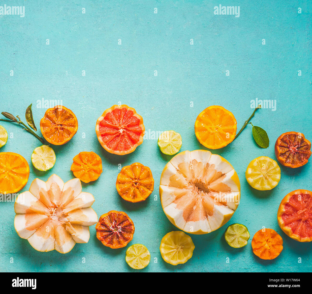 Various colorful citrus fruits halves with green leaves on light blue ...