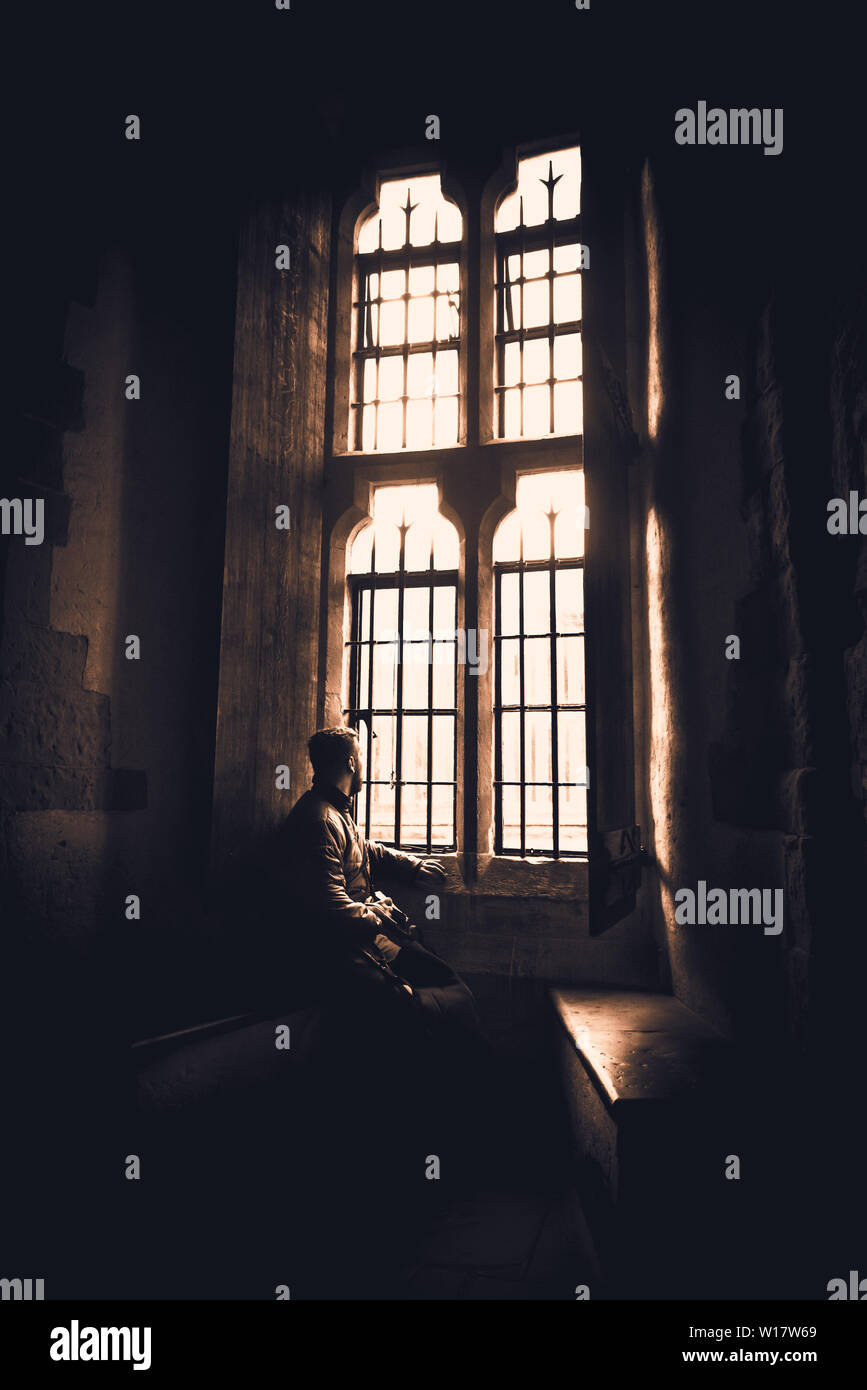 Rear view at silhouette of man sitting in the darkness looking through ...