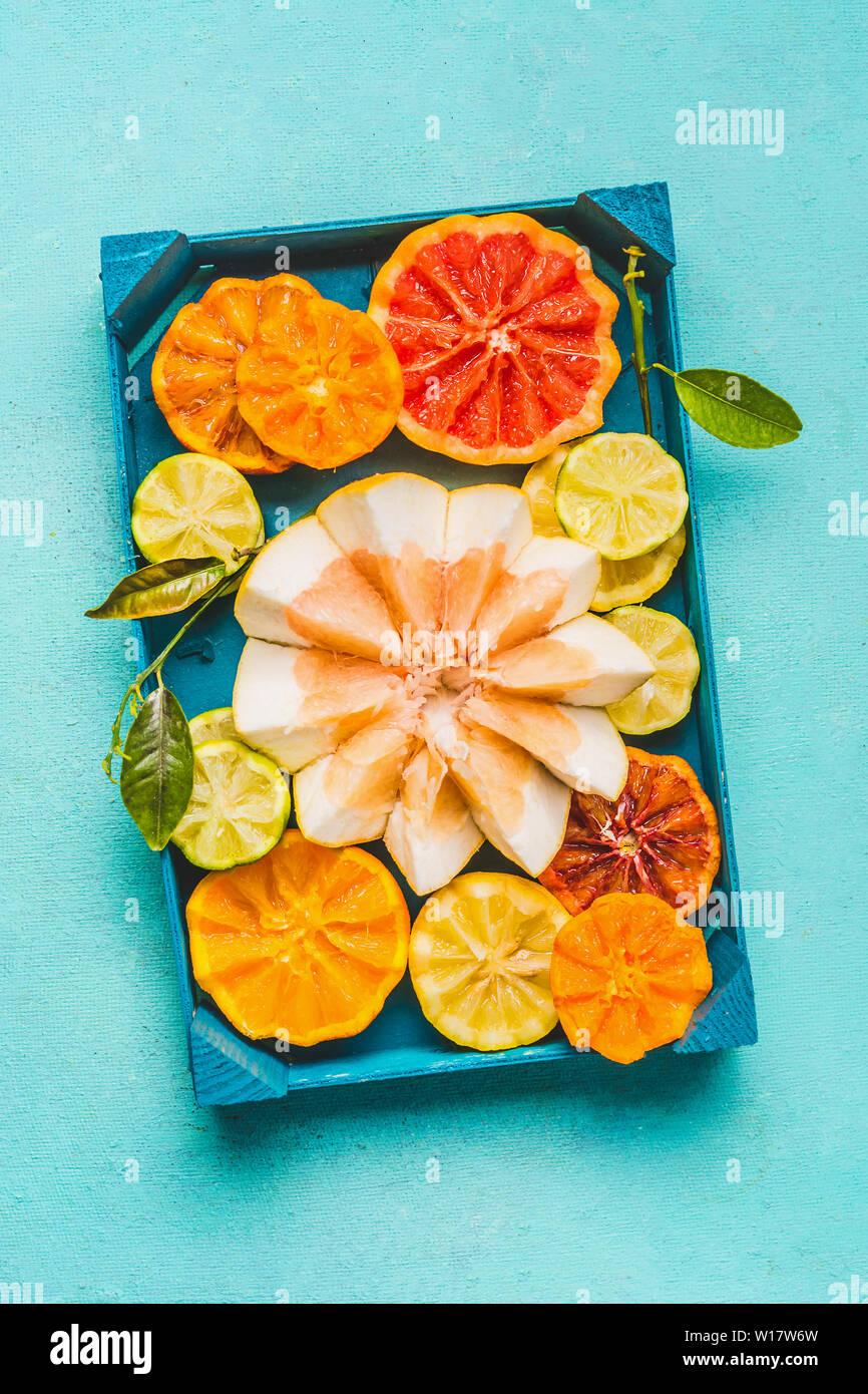 Various colorful citrus fruits halves with green leaves in wooden tray ...