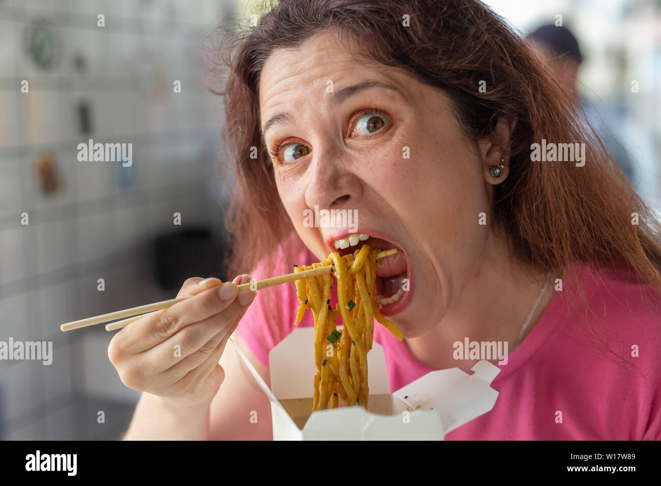 Close-up portrait of an amusing crazy young pretty girl eating udon ...