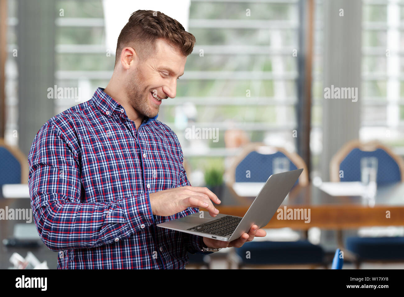 Young man standing, holding laptop computer, working Stock Photo - Alamy