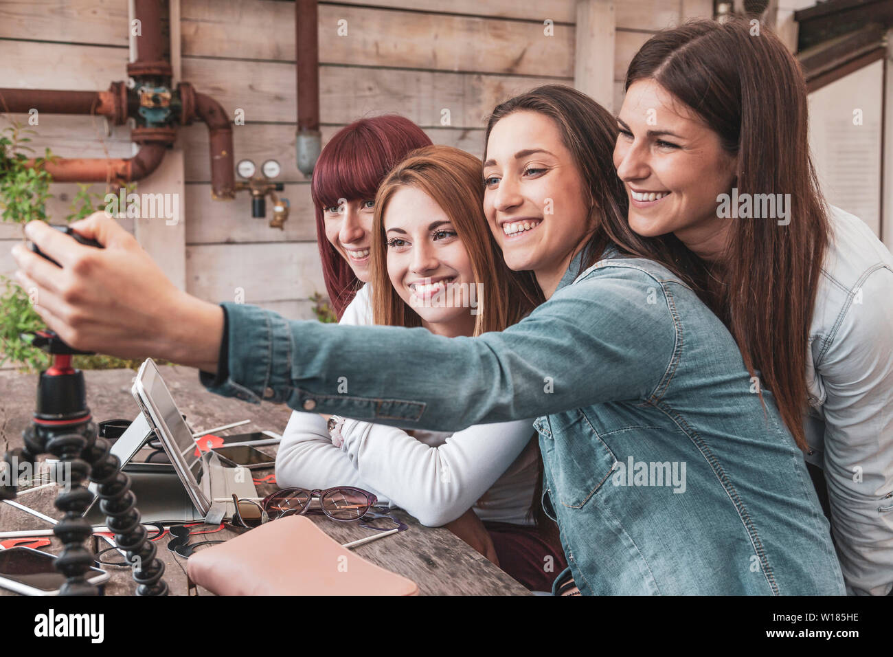 four young vloggers take a selfie with a camera leaning against a small ...