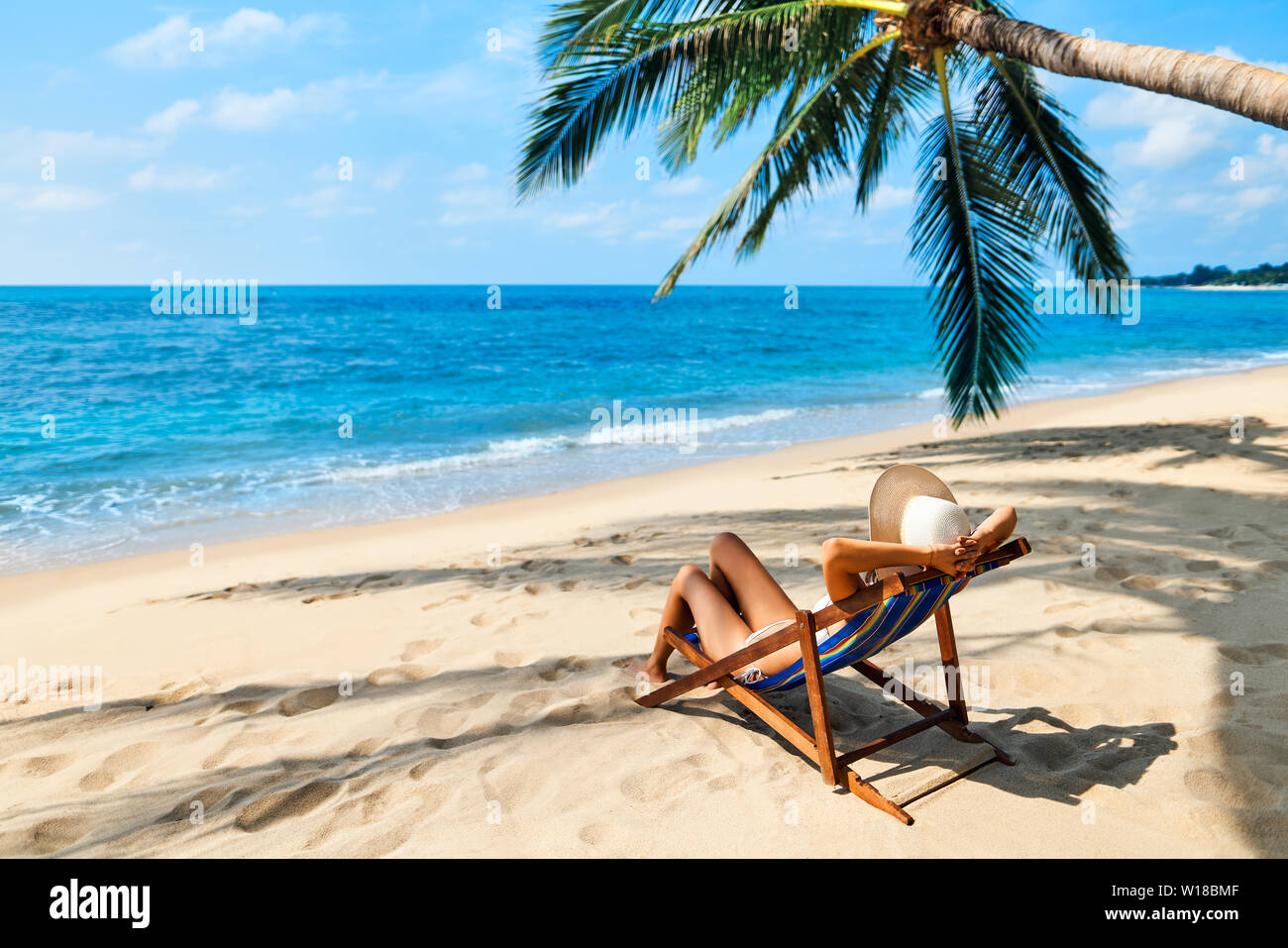 Back view of young beautiful woman sunbathe and relax on tropical beach ...